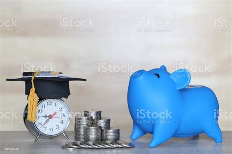 나무 배경에 알람 시계에 동전 돈과 졸업 모자의 스택 블루 돼지 저금통 교육 개념에 대한 돈을 절약 개념에 대한 스톡 사진 및