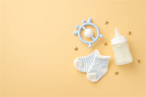 아기 액세서리 개념 파란 딸랑이 작은 양말 우유 병과 카피 스페이스가있는 고립 된 파스텔 베이지 색 배경에 금색 별의 탑 뷰