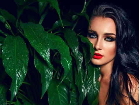 یک دختر برنزه زیبا با آرایش طبیعی و موهای خیس در جنگل در میان گیاهان