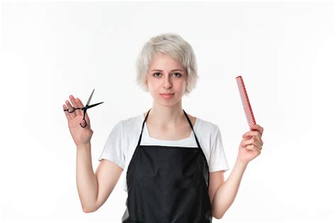 흰색 티와 검은 앞치마에 예쁜 미용사는 흰색 배경에 고립 된 작업에 대한 준비가 검은 가위와 빨간 헤어 브러시를 들고 뷰티 산업