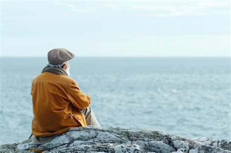 Premium Photo Elderly Man Sitting On A Rock Gazing At A Tranquil Sea