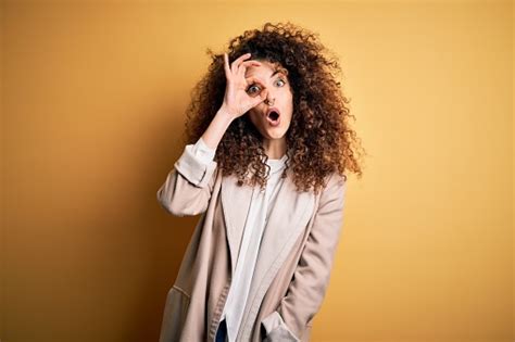 곱슬 머리와 피어싱 캐주얼 티셔츠와 Diadem을하고 확인 제스처를하고 젊은 아름다운 갈색 머리 여자는 놀란 얼굴로 충격 눈을 통해 손가락을 통해 보고 믿을 수 없는 표현