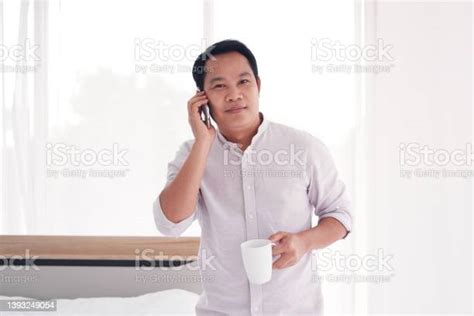 흰색 셔츠를 입고 웃고 있는 아시아 사업가가 스마트폰으로 전화를 걸고 이야기하고 있습니다 그는 사무실에서 창 근처 아침에 뜨거운