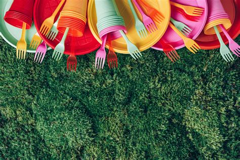 일회용 플라스틱 식기 접시 포크 숟가락 녹색 잔디 이끼 배경에 컬러 플라스틱 일회용 식기 맨 위 보기입니다 공간을 복사합니다 생일 피크닉 기구 플라스틱 및 생태 재활용