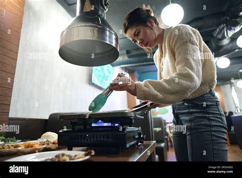 Asian Woman Cooks Meat Into The Skillet On The Stove In The Reas Stock