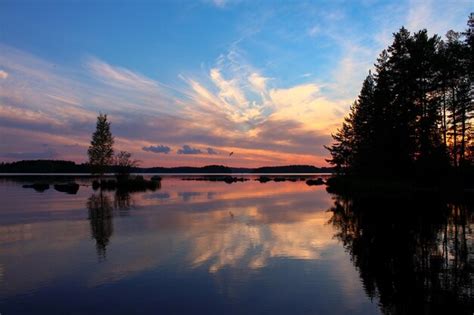 Una puesta de sol sobre un lago con algunos árboles y un cielo con