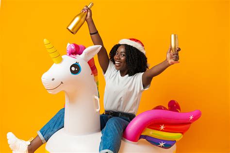 스튜디오에서 산타클로스 모자를 쓰고 무지개 유니콘 플로트에 앉아 있는 아프리카 여성 20 24세에 대한 스톡 사진 및 기타 이미지 20 24세 노란색 배경 다중 색상