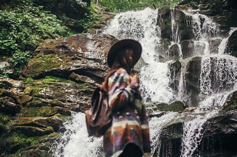 산에 숲에 폭포 보고 배낭 모자에 세련 된 Hipster 소녀 여행자 여자 숲 탐험입니다 여행과 방 랑 벽 개념입니다 폭포에