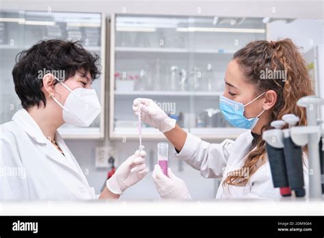 Two Young Female Scientists Wearing Face Masks During An Experiment In A Lab Laboratory