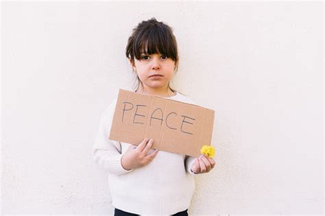 진지하고 반전 운동가 어린 소녀가 평화와 노란 꽃이라는 표지판을 들고 있습니다 전쟁 대결 행동주의 평화와 사랑의 개념