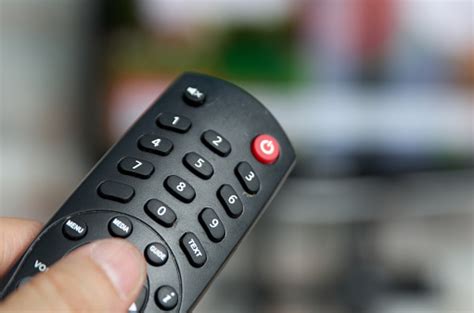 Tv 프로그램 변경 Tv 화면이있는 흐릿한 배경에서 Tv 리모컨을 들고 인간의 손을 클로즈업하십시오 리모콘에 대한 스톡 사진 및