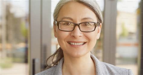 출근길에 아름답고 행복한 선배 여성 노트북을 들고 사무실 건물 근처에 서 있는 동안 카메라를 향해 웃고 있는 비즈니스 여성의 수직 사진 사업가 일 개념 사진