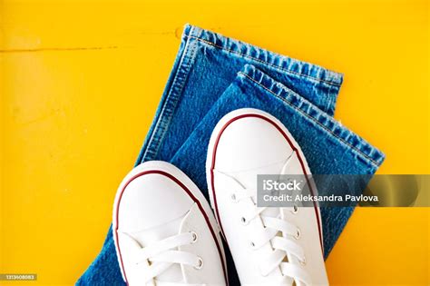 밝은 노란색 배경에 고무 밑창과 파란색 청바지에 흰색 끈이 있는 흰색 새로운 클린 스니커즈 세련된 의류 콘텐츠 선택적 초점