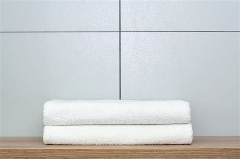 깔끔하게 접힌 흰색 수건 두 개가 세라믹 타일을 배경으로 나무 선반위에 놓여 있습니다 수건에 대한 스톡 사진 및 기타 이미지
