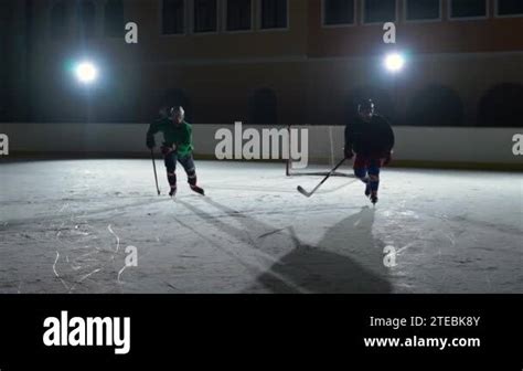 Two Men In Uniforms And Helmets With Hockey Sticks Skate On Ice Arena