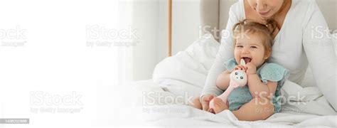웃는 엄마와 아기 소녀는 침대에 누워 함께 시간을 즐기고 있습니다 가족 시간 개념입니다 장난감을 가지고 노는 재미 모의 복사