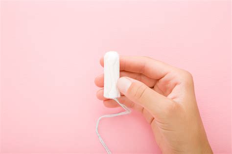 밝은 분홍색 테이블 배경에 새로운 흰색 위생 탐폰을 들고 젊은 성인 여성 손 파스텔 색상 근접 촬영 여성 위생 하향 보기 체내형
