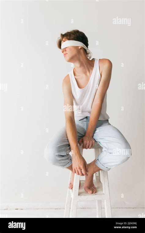 Portrait Of Young Man With Blindfold Sitting On Chair Isolated On White