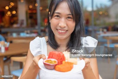 아침 식사를 먹는 여자 계란 베네딕트 수박 파파야 멜론 열정 과일 오렌지 주스 및 커피와 같은 과일 회색 플레이스매트 위에 놓음