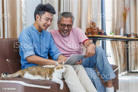 아시아 수석 아버지 와 그의 성인 아들 사용 디지털 태블릿 와 그의 고양이 앉아 에 소파 에 거실 에 홈 아버지에 대한 스톡
