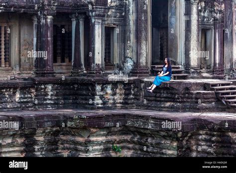 A Tourist Sits Among The Massive Stone Structures At The Ancient Angkor Wat Temple Complex In