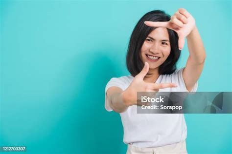 초상화 아시아 아름다운 행복한 젊은 여자 미소 흰색 치아 는 손과 손가락으로 창의력 사진 프레임을 만드는 흰색 티셔츠를 착용
