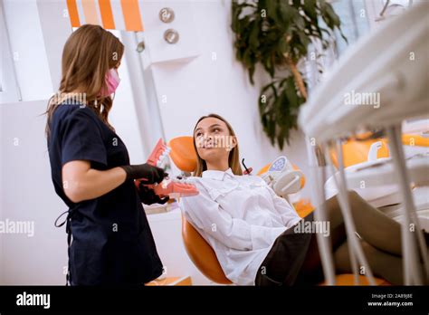 Pretty Young Female Dentist Explaining To Female Patient Cleaning Tooth