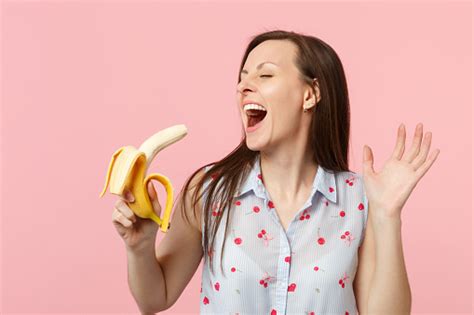 분홍색 파스텔 벽 배경에 고립 된 신선한 잘 익은 바나나 과일을 들고 눈을 유지 하는 여름 옷에 젊은 여자를 웃 고 사람들은