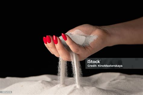 손에 하얀 마른 모래를 한 줌 들고 검은 색 스튜디오 배경에 손가락을 통해 모래를 쏟아 부은 여성 삶의 흐름의 개념 여성의 손에