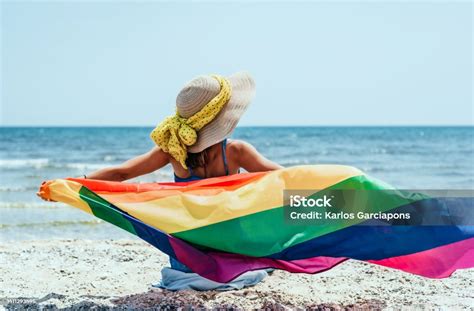 바다를 향한 노란 모자와 머리 스카프를 가진 여자는 양손으로 무지개 깃발을 들고 있습니다 그녀는 등을 돌렸다 다양성과 관용 개념 Lgbt 여성 동성애자 남성 동성애자 50