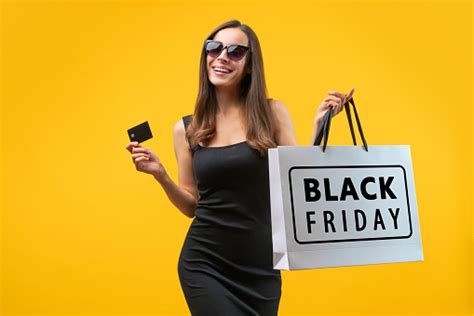 트렌디 한 검은 드레스 Ans 안경을 착용하고 신용 카드 Ans Black Friday 쇼핑 백을 손에 들고 밝은 색상의 노란색
