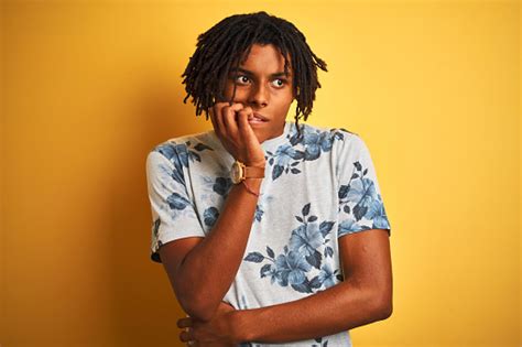 고립 된 노란색 배경 위에 여름 꽃 티셔츠를 입고 공포를 가진 아프로 남자는 입에 물린 손톱에 손으로 스트레스와 긴장 찾고 불안 문제 T 셔츠에 대한 스톡 사진 및 기타