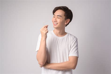 하얀 배경 스튜디오 치과 건강 관리 및 교정 개념 위에 눈에 띄지 않는 중괄호를 들고있는 젊은 미소 짓는 남자 건강관리와 의술에