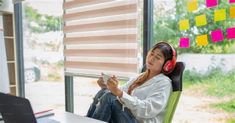 헤드폰으로 음악을 듣고 노트북 컴퓨터를 사용하고 사무실에서 커피를 마시는 젊은 아시아 여성의 초상화 사진 Unsplash의