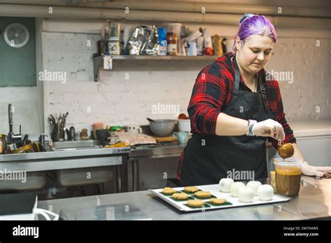 Concentrated Female Pastry Chef In Black Apron Decorating Desserts In