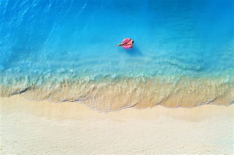 여름의 석양에 파도와 맑은 푸른 바다에서 도넛 수영 반지와 수영 하는 젊은 여자의 공중 보기 소녀 푸른 물 모래 해변과 열 대 공중 풍경입니다 평면도 여행 공중 뷰에 대한