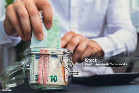 남자는 계산기에 돼지 저금통에 있는 유리병에서 유로 현금의 비용 지폐를 세고 있다 알아볼 수 없는 사업가의 손을 닫습니다 예산 투자 개념을 절약하십시오 유로 펀드 저축
