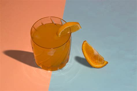 파스텔 블루 오렌지 배경에 그림자가있는 오렌지 주스 한 잔과 유리 옆에있는 오렌지 조각 창조적 인 여름 디자인 각얼음에 대한