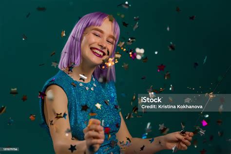 녹색 배경에 색종이 비 아래 빛나는 벵골 화재 춤과 힙스터 여자 크리스마스 휴가 개념 어린 염색 보라색 머리 소녀 와 스파클러 축하 미소 시간을 즐기는 미소에 대한 스톡