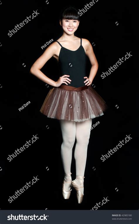 A Young Asian Ballerina Standing On Tip Toe Against Black Background