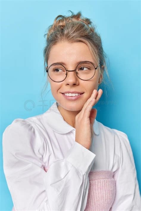 背景高清图片 忧郁的美丽女学生的垂直镜头表情巧妙轻轻抚摸脸颊若有所思地看着远处戴着圆形眼镜白色衬衫与蓝色背景隔离 产品实拍免费下载
