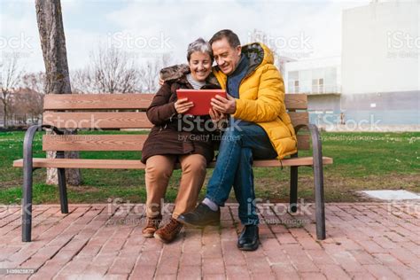 공원의 벤치에 앉아 태블릿으로 비디오를 보는 두 성인의 얕은 초점 2명에 대한 스톡 사진 및 기타 이미지 2명 공원 공원