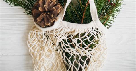 흰색 소박한 배경에 녹색 가문비나무 가지와 솔방울이 있는 재사용 가능한 면 가방 겨울 장식 제로 폐기물 휴일과 그물 쇼핑백 텍스트 공간이 있는 상위 뷰 사진