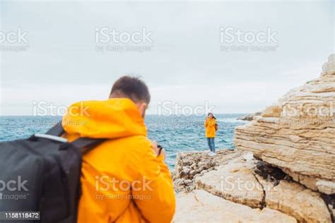 바다 근처 절벽에서 노란 비옷을 입은 여성의 사진을 찍는 남자 2명에 대한 스톡 사진 및 기타 이미지 2명 가장자리 걷기