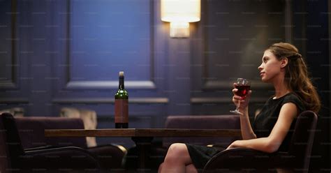 검은 드레스를 입은 예쁜 젊은 여자가 테이블 옆 안락의자에 앉아 혼자 레드 와인 한 잔을 마신다 사진 Unsplash의