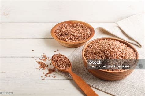 광택이 없는 현미와 나무 숟가락이 흰색 나무 배경과 린넨 직물에 새기있는 두 개의 나무 그릇 측면 도면 복사 공간 0명에 대한