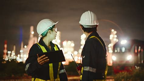 안전 유니폼을 입은 두 명의 아시아 석유화학 엔지니어가 디지털 태블릿과 노트북을 들고 야간 근무를 하며 정유 공장의 공정 품질을 검사하고 있습니다 2명에 대한 스톡 사진 및