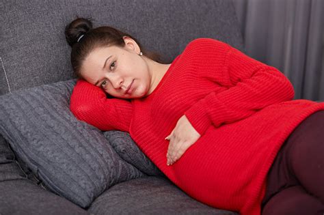 졸린 피곤한 임신한 여자의 이미지는 낮잠 배꼽에 손을 유지 차분한 분위기를 즐기는 빨간 스웨터를 입고 아늑한 Woom에 회색