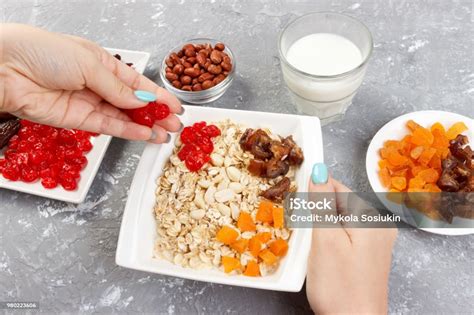 여자는 아침 식사에 대 한 그녀의 Muesli를 준비 하 고 여자 자신 말린 과일 오트밀 죽에 넣습니다 회색 배경 평면도에 유용 하 고 건강 한 아침 식사 가정의 방에 대한