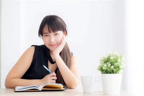 아름 다운 젊은 아시아 여자 앉아 연구 웃 고 글 노트북 학습과 생활 집에서 여자 숙제 작업 테이블 교육 개념을 비즈니스 여자